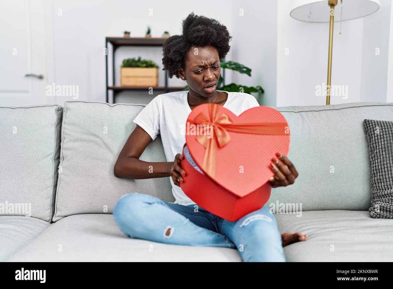 African young woman opening romantic gift in shock face, looking ...