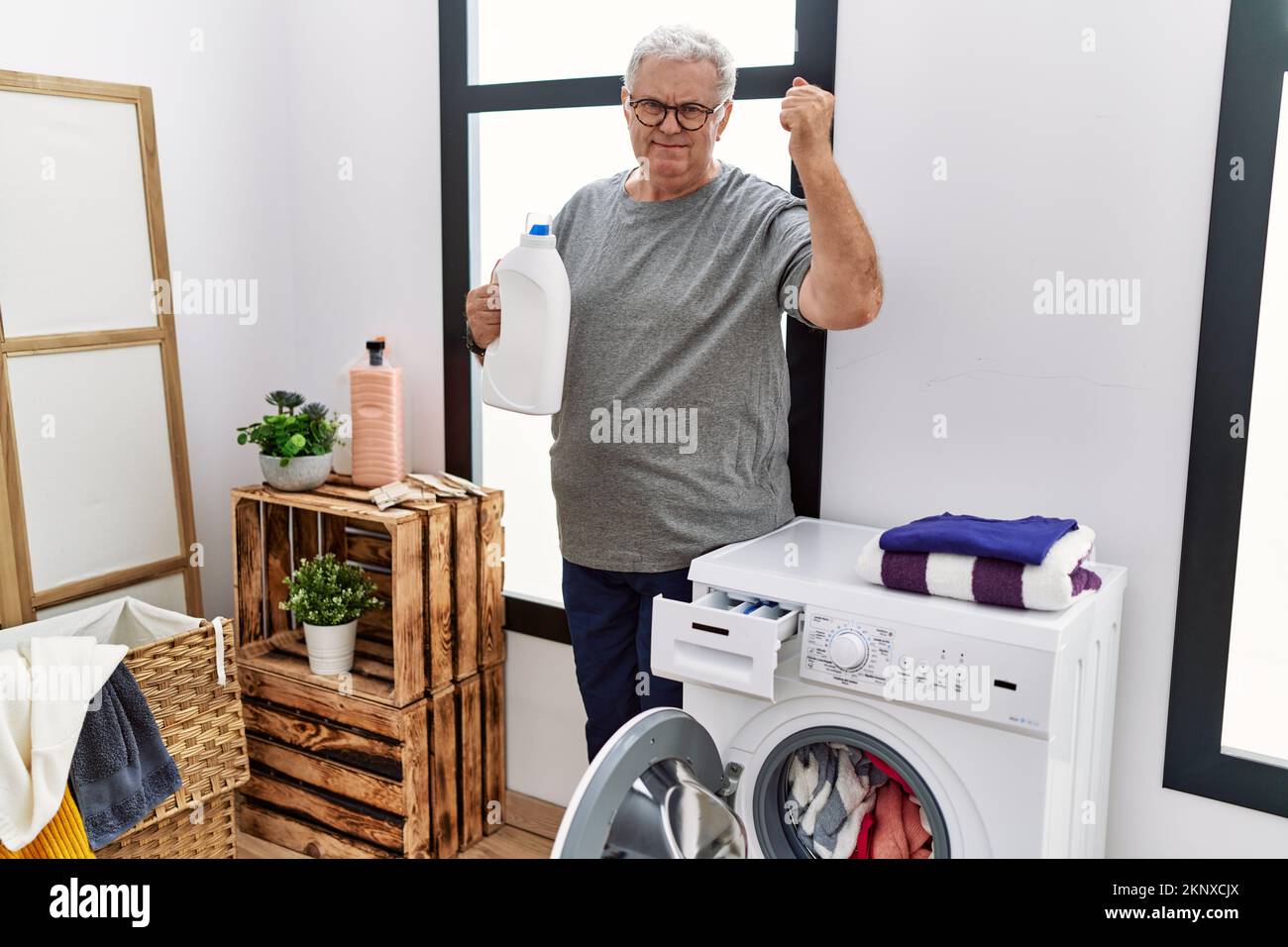 Senior caucasian man doing laundry holding detergent bottle annoyed and ...