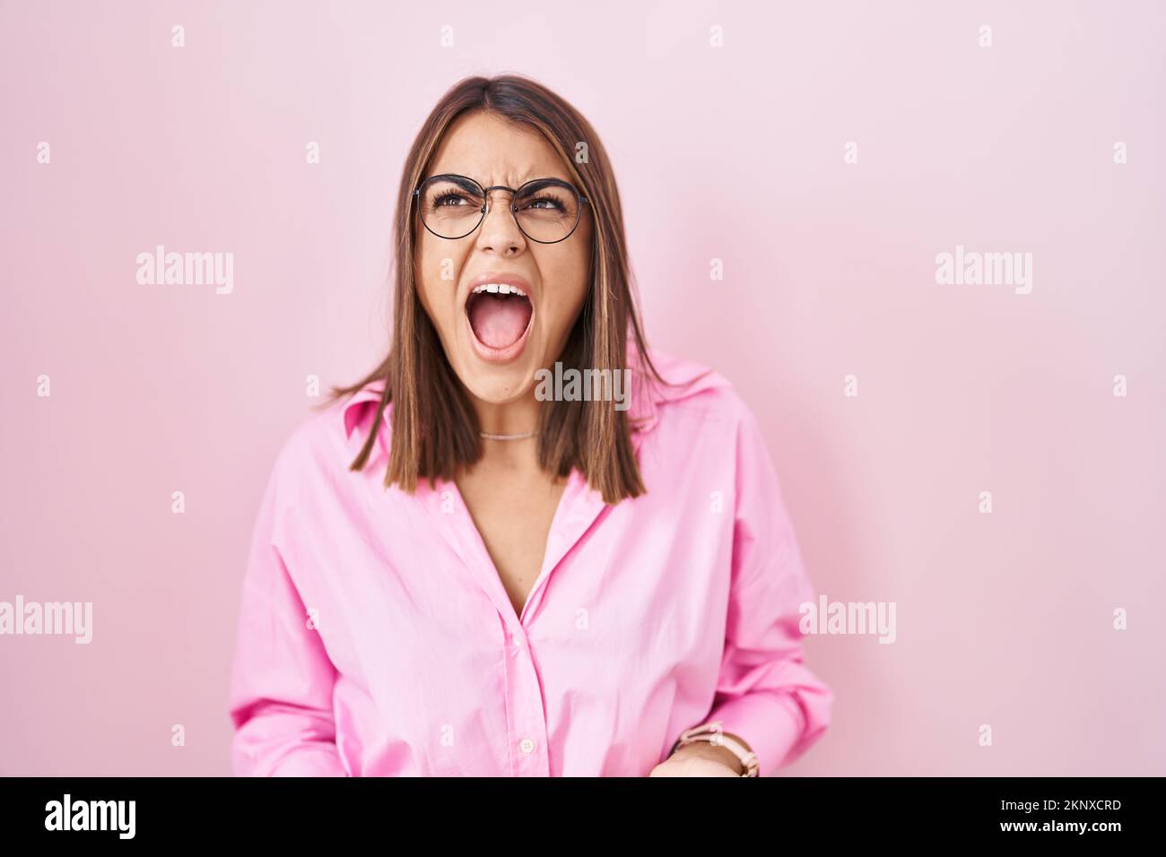 Young hispanic woman wearing glasses standing over pink background ...