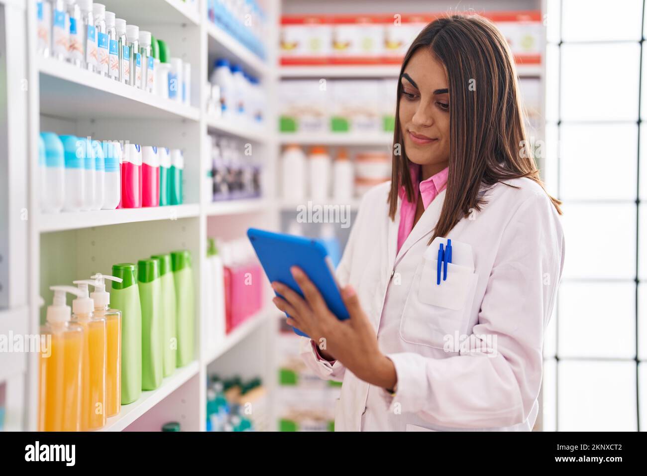 Young beautiful hispanic woman pharmacist using touchpad working at ...