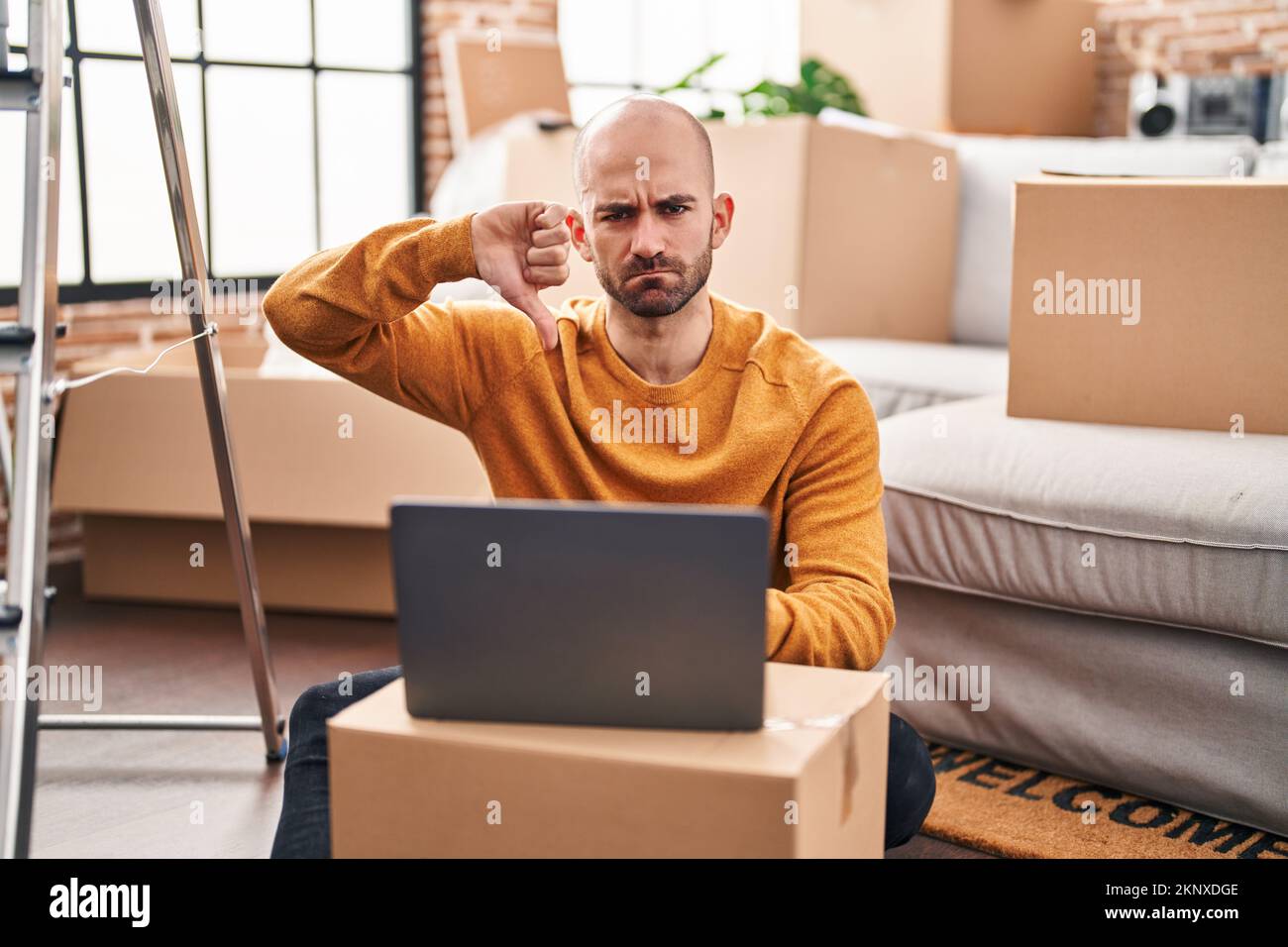 Young bald man with beard moving to a new house using laptop with angry ...