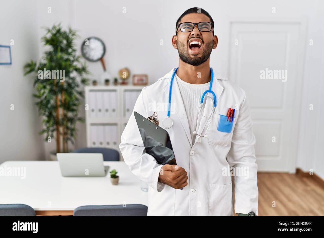 Young indian man wearing doctor uniform and stethoscope angry and mad ...