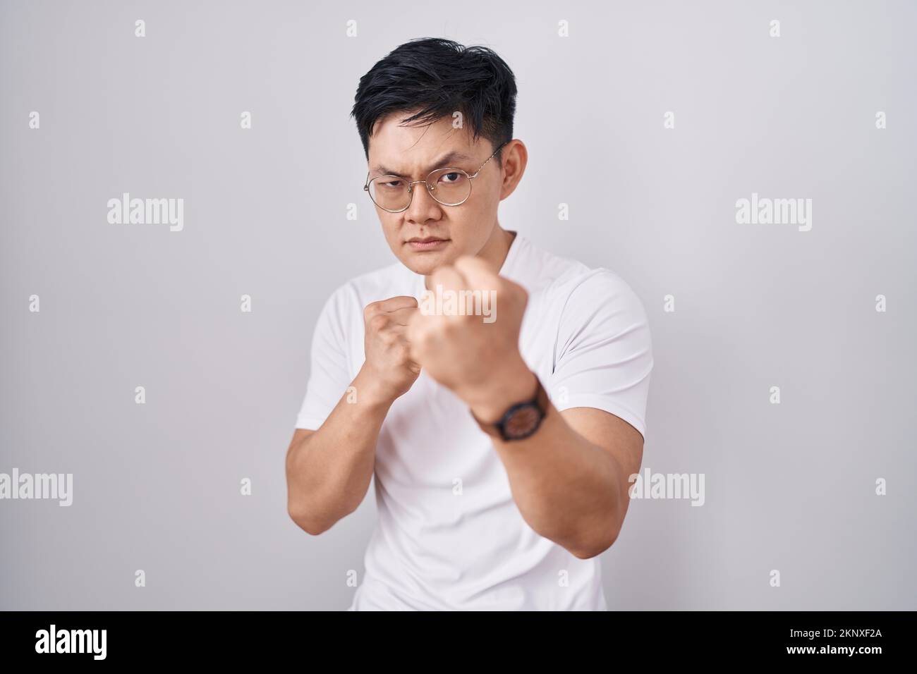 Young asian man standing over white background ready to fight with fist ...