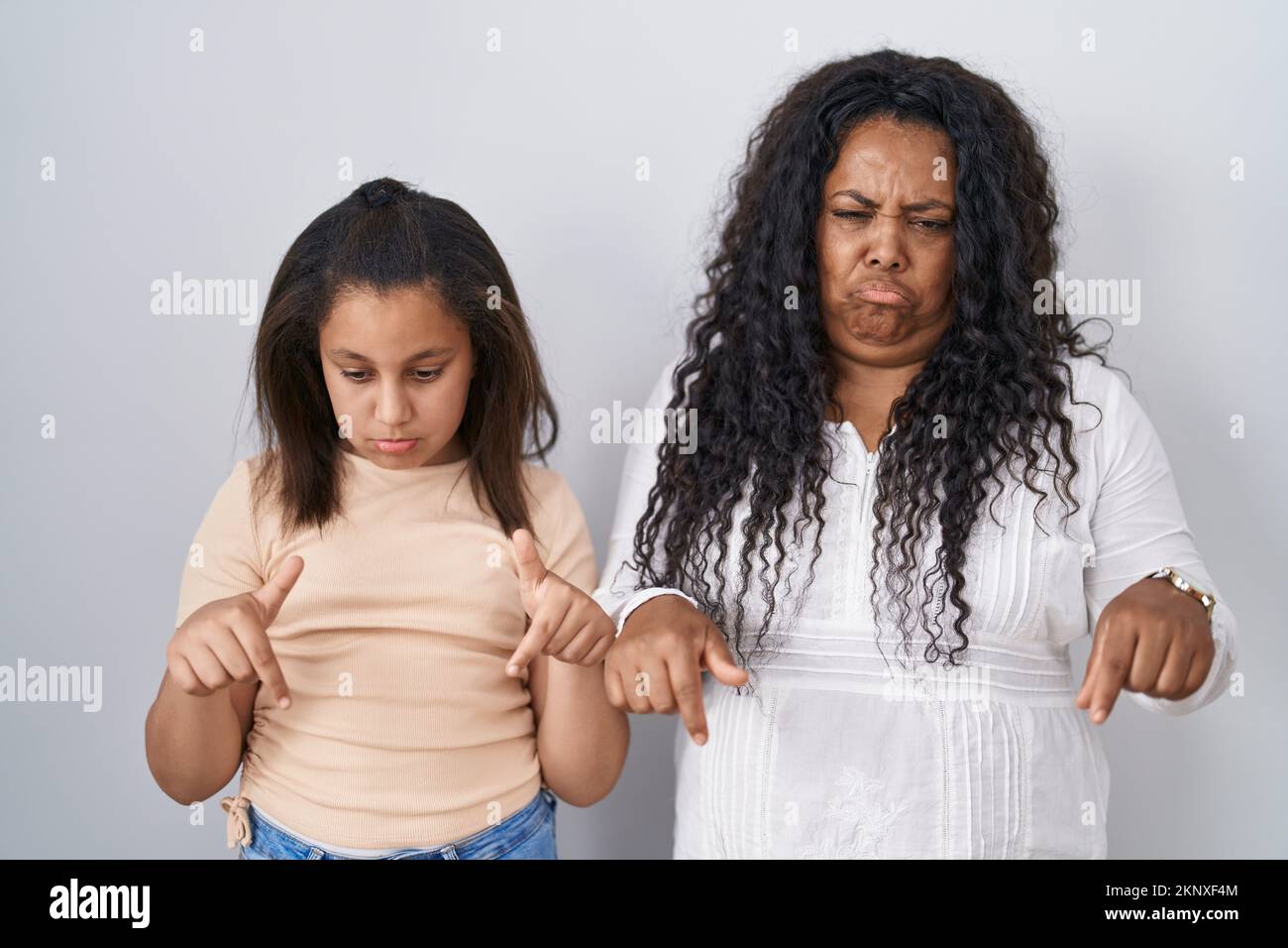Mother and young daughter standing over white background pointing down ...