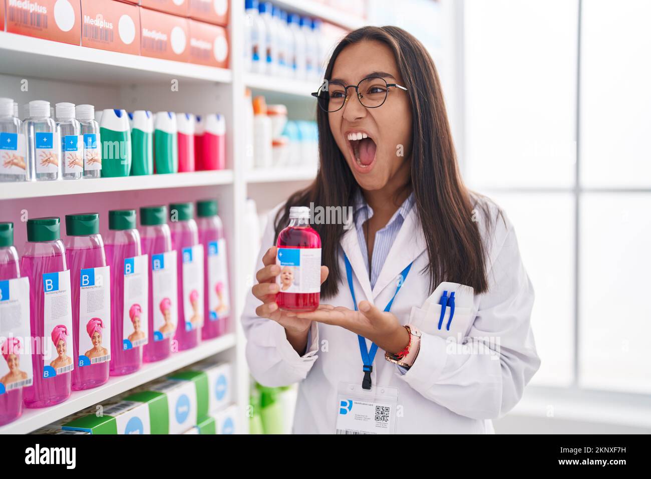 Young hispanic woman working at pharmacy drugstore holding syrup angry ...