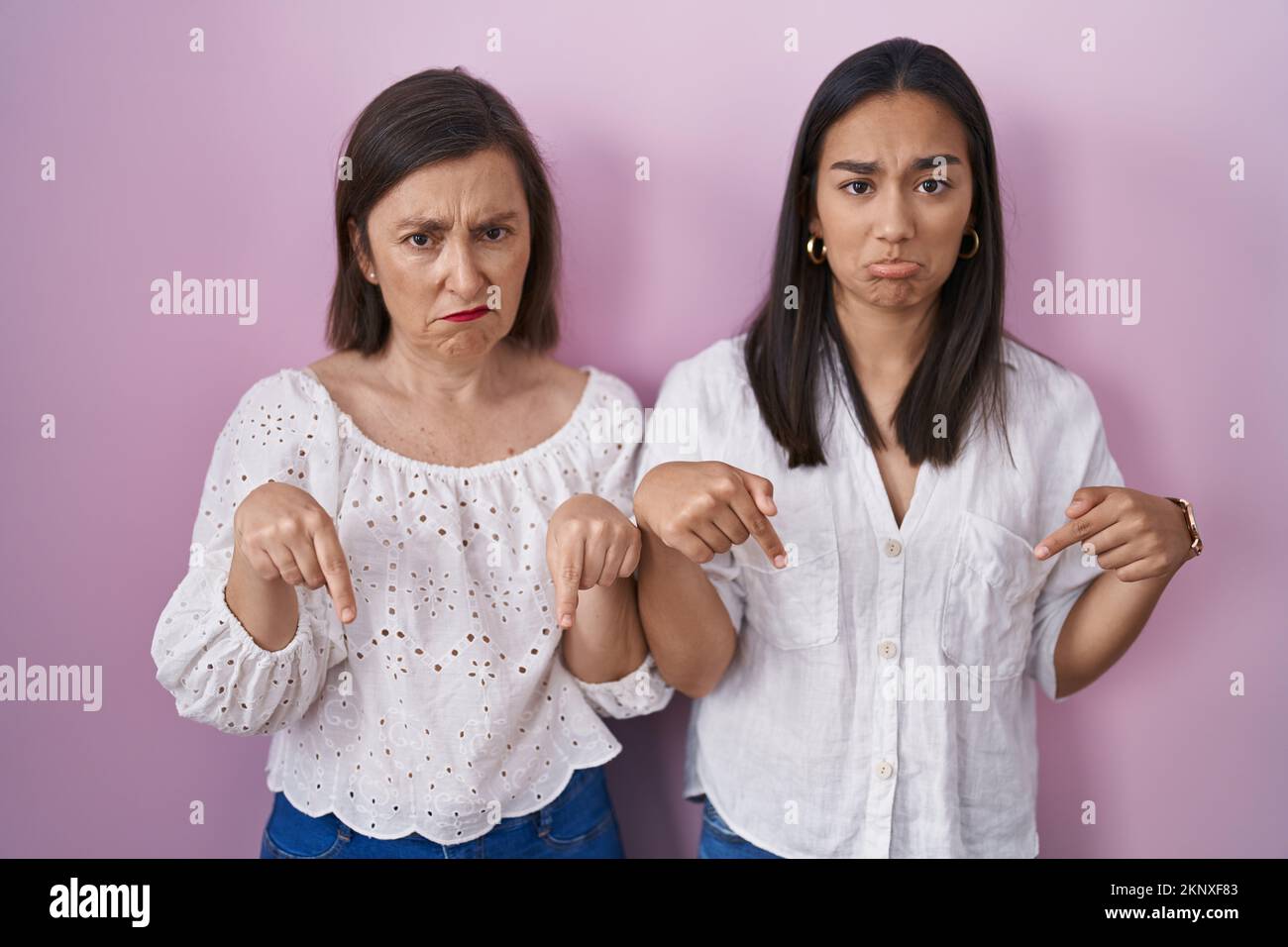 Hispanic mother and daughter together pointing down looking sad and ...