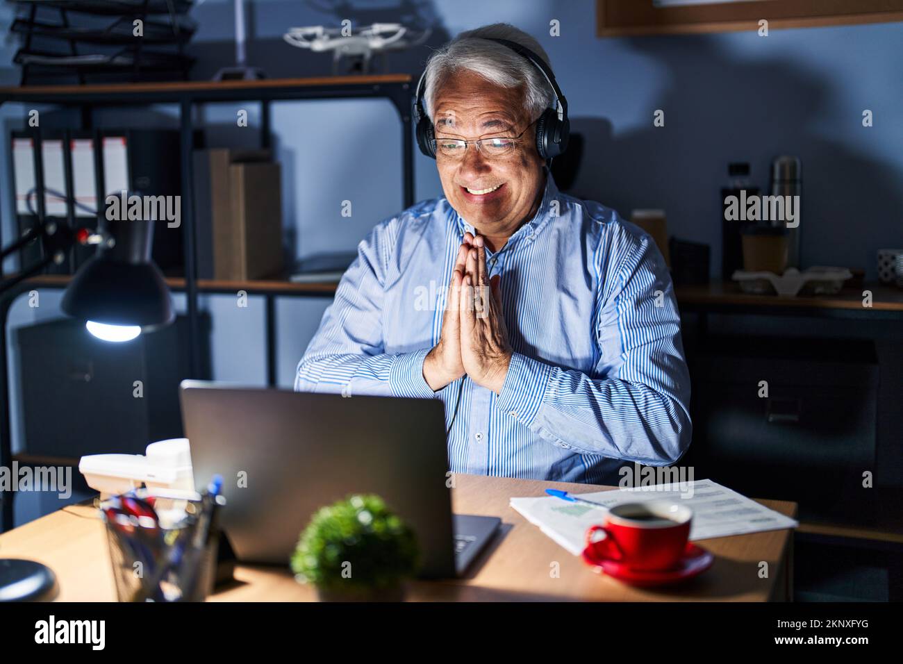 Hispanic senior man wearing call center agent headset at night praying ...