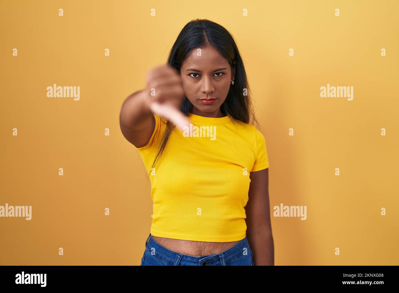 Young indian woman standing over yellow background looking unhappy and ...