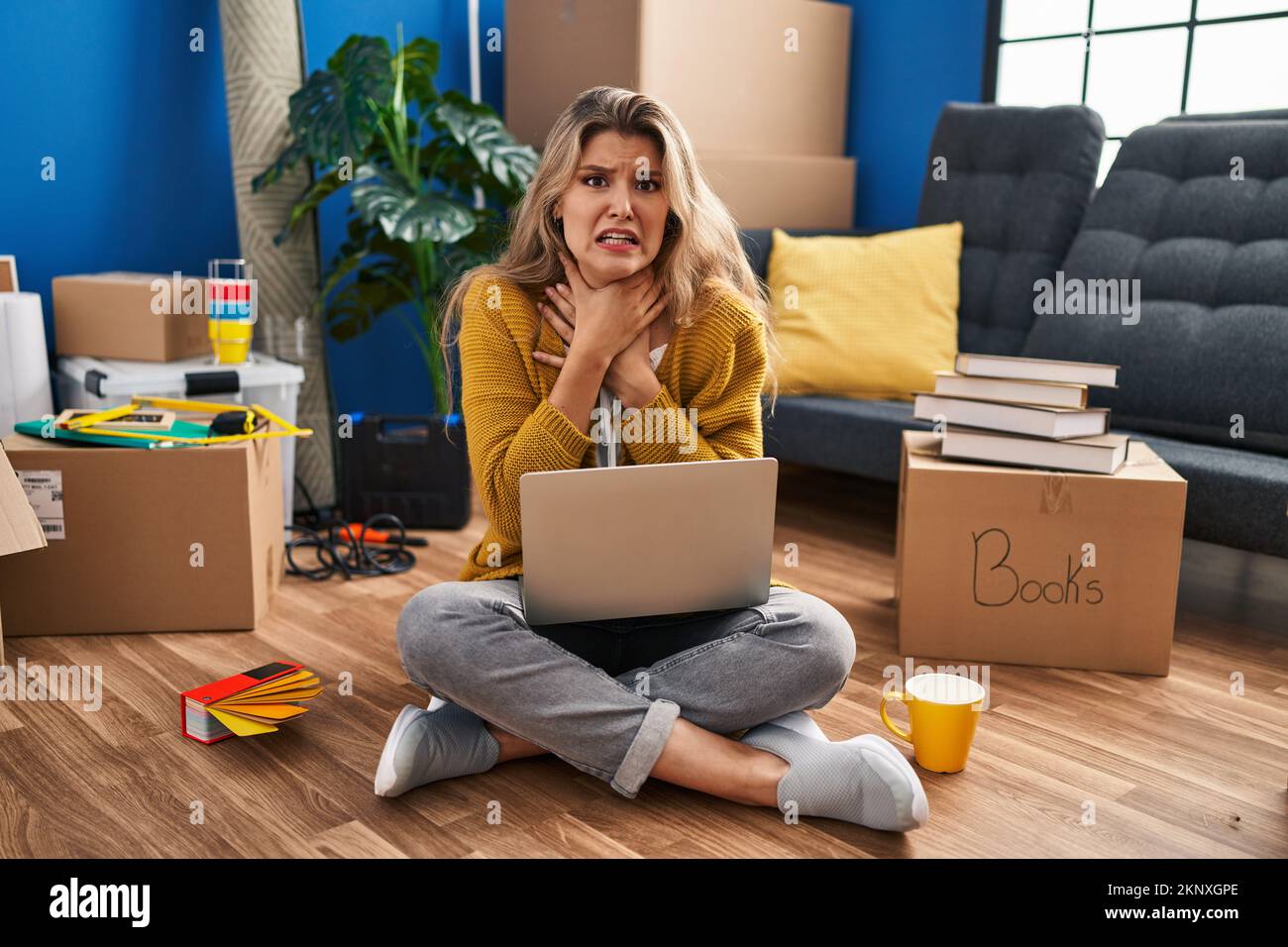Young woman sitting on the floor at new home using laptop shouting and ...
