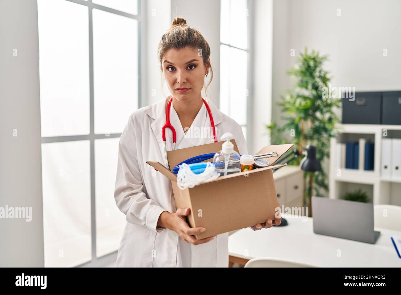 Young doctor woman holding box with medical items skeptic and nervous ...