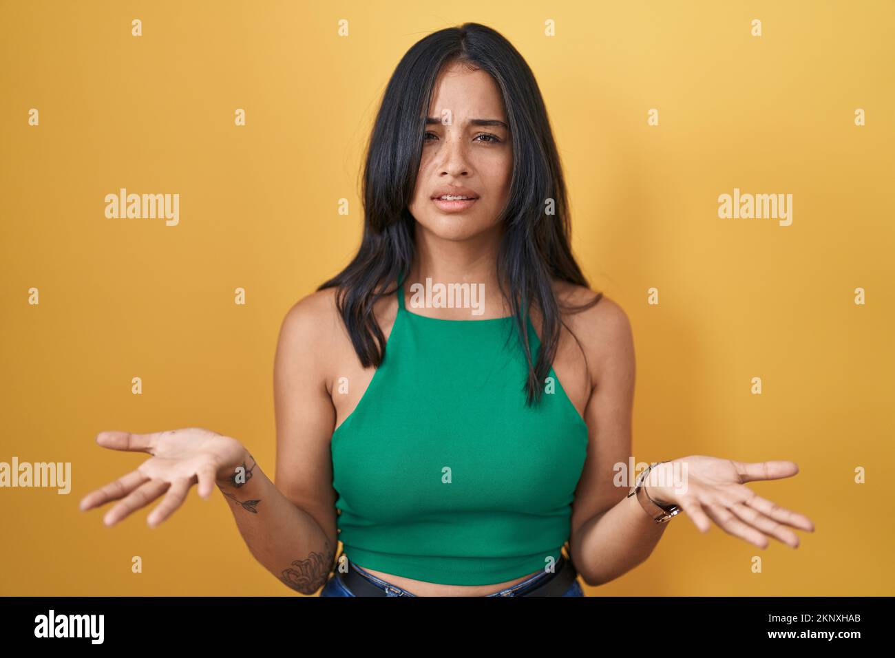 Brunette woman standing over yellow background clueless and confused ...