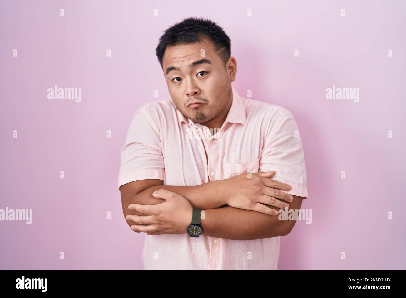 Chinese young man standing over pink background shaking and freezing ...