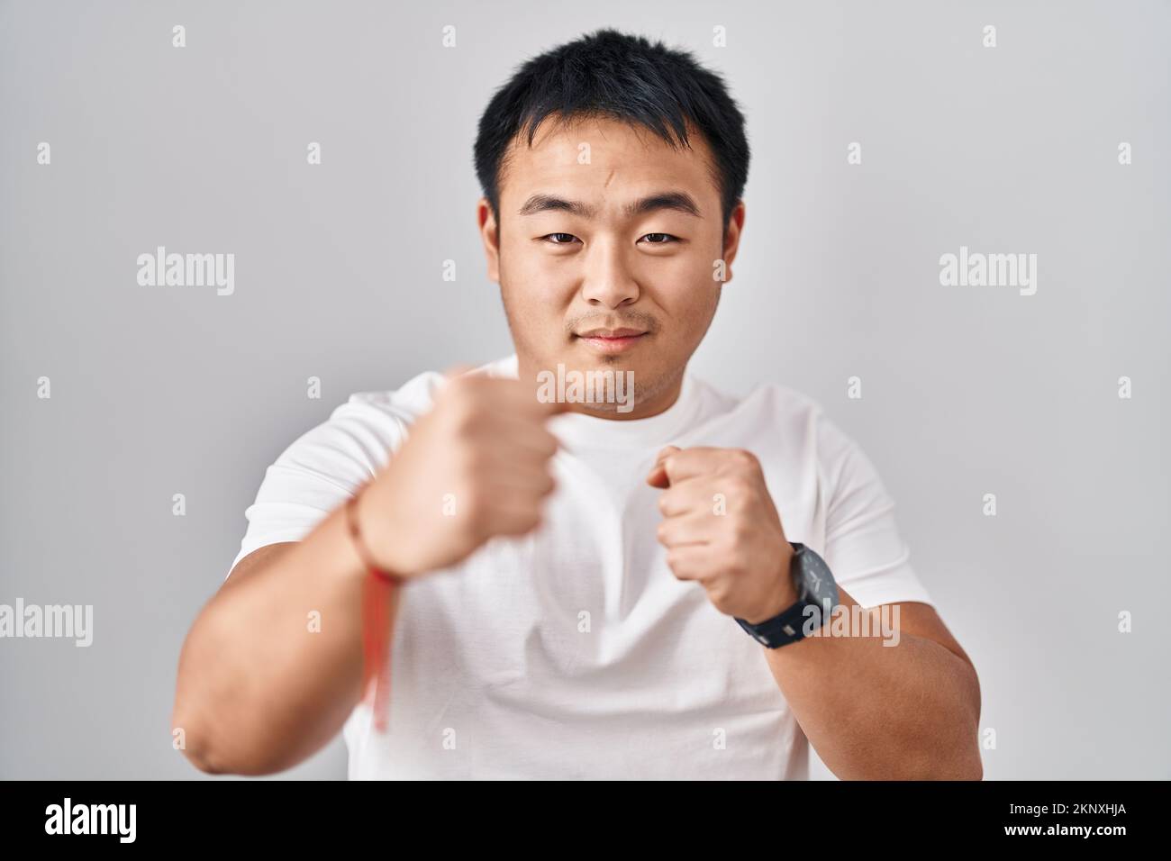 Young chinese man standing over white background ready to fight with ...