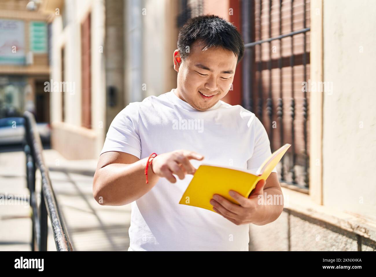 Young chinese man smiling confident reading book at street Stock Photo ...