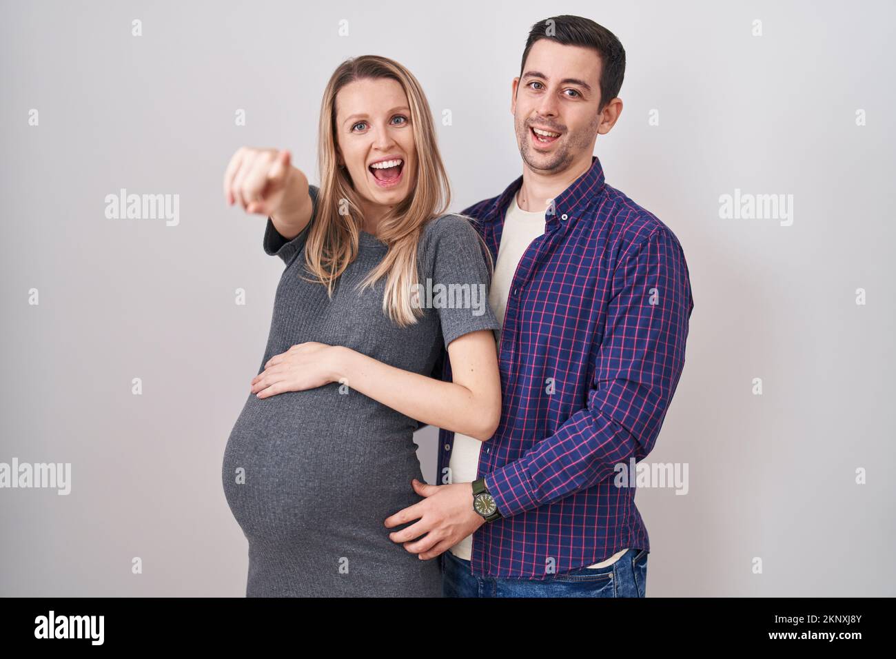 Young couple expecting a baby standing over white background pointing ...