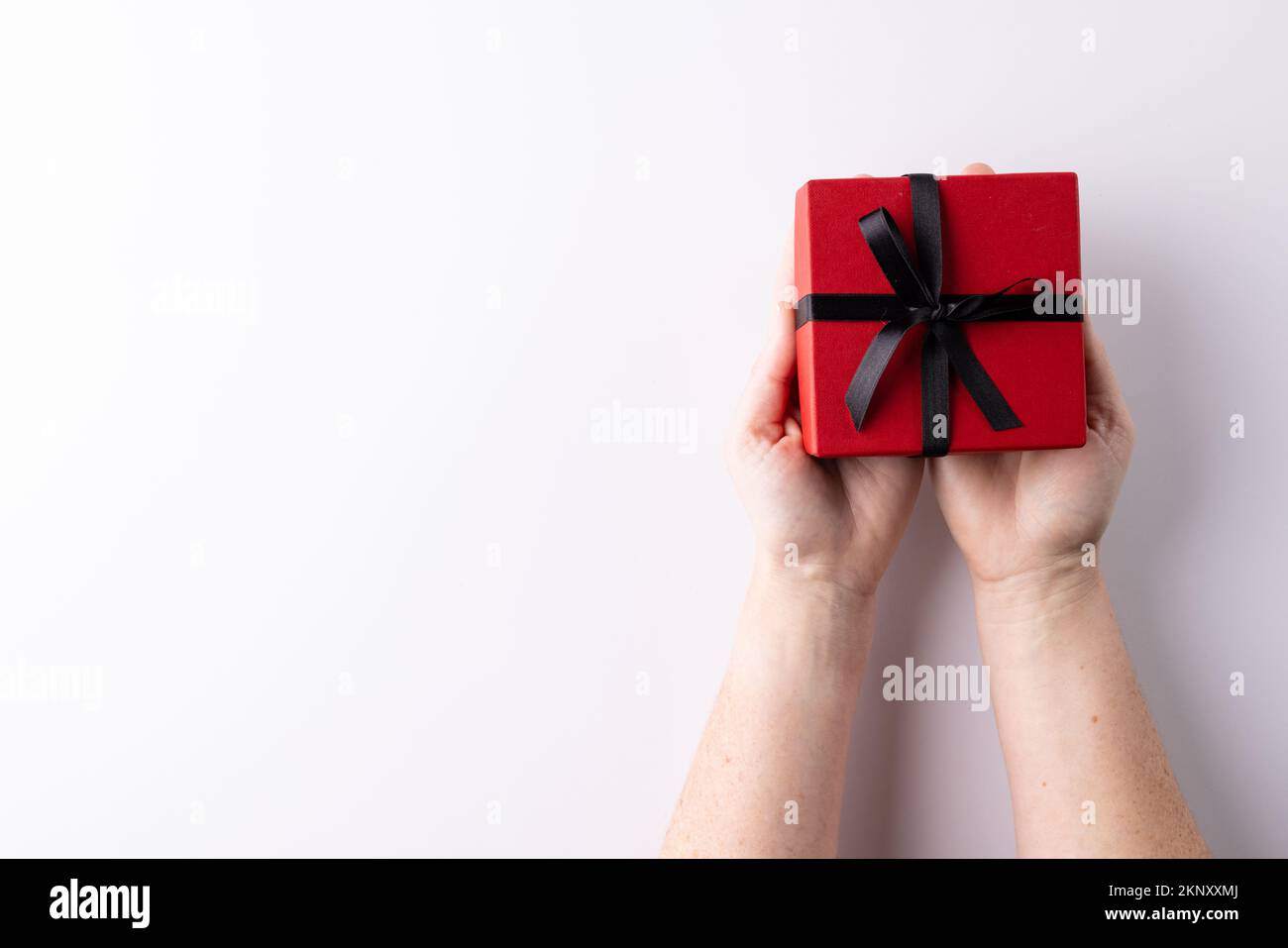 Hands holding red gift box tied with black ribbon, on white background with copy space Stock ...