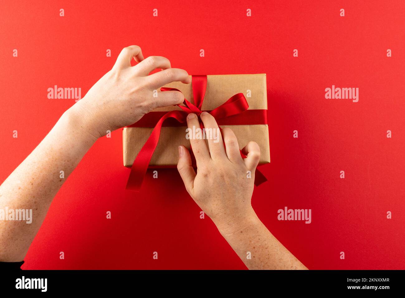 Overhead of hands tying gift in brown paper with red ribbon, on red ...