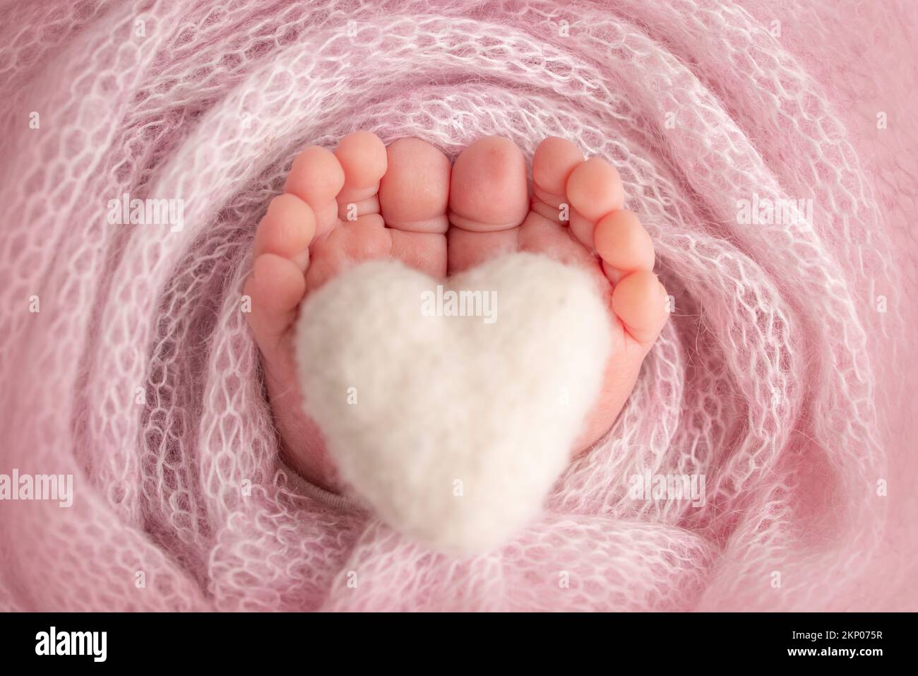 Knitted white heart in the legs of a baby. Soft feet of a new born in a ...