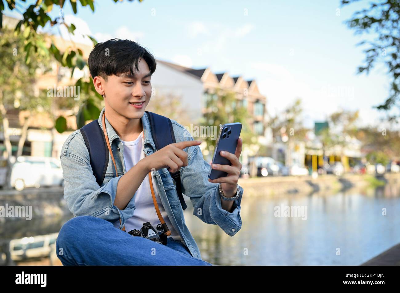 Happy and handsome young Asian male tourist using his smartphone while ...