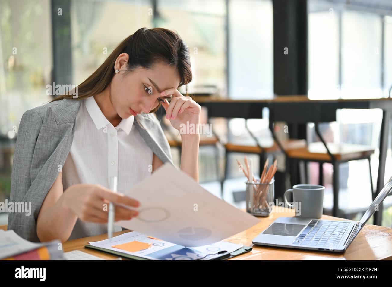 Stressed and serious millennial Asian businesswoman or female manager examining financial report ...