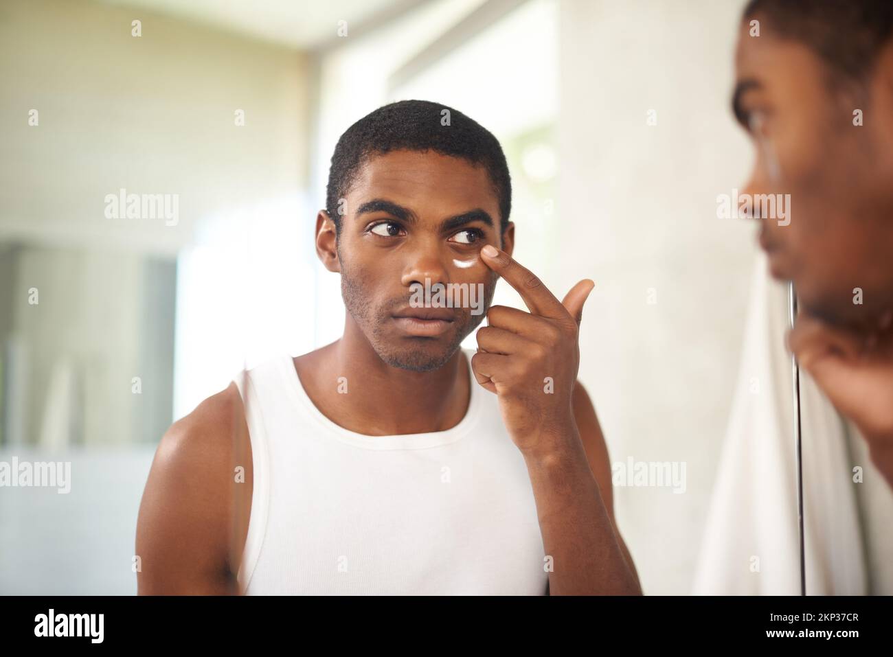 He takes care of his skin. A young man applying cream to his face while ...