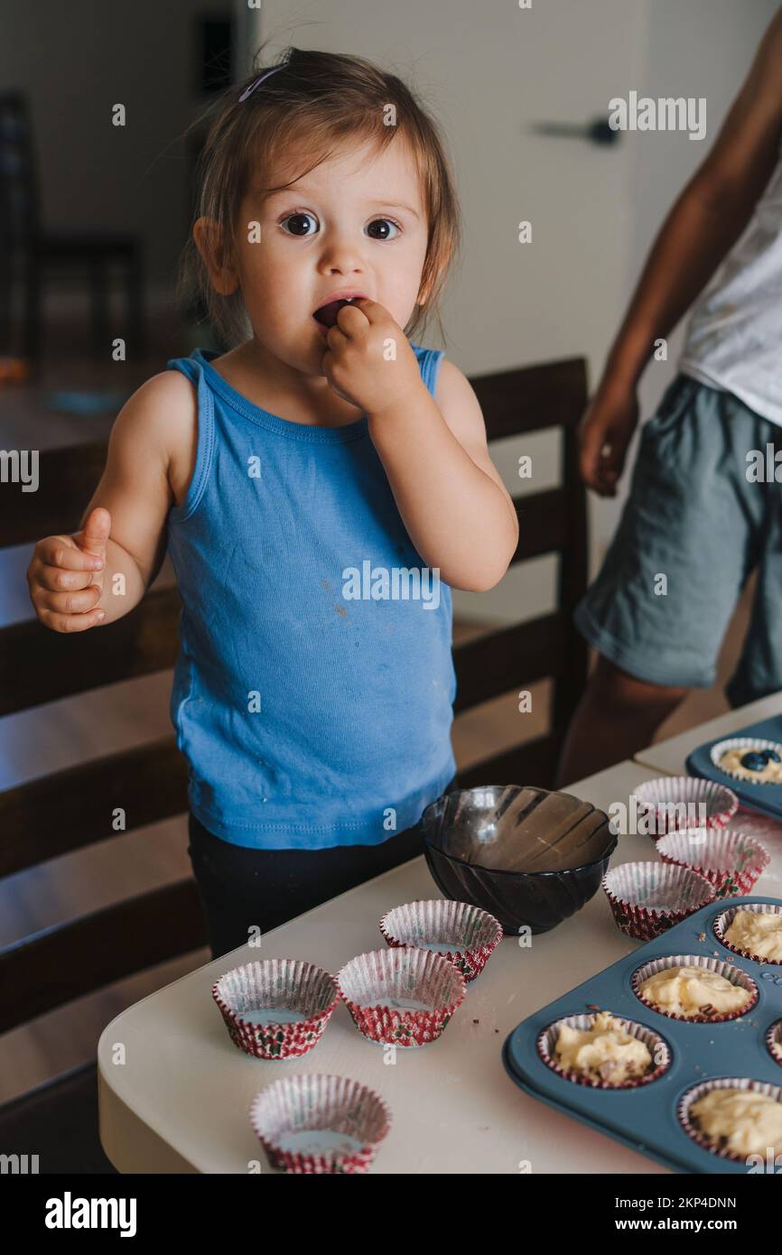 Baby girl looking at the camera while placing cupcake forms in baking ...
