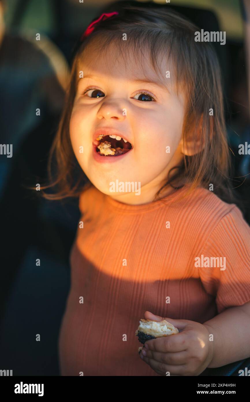View through the open car window of a baby girl eating a pie while the ...