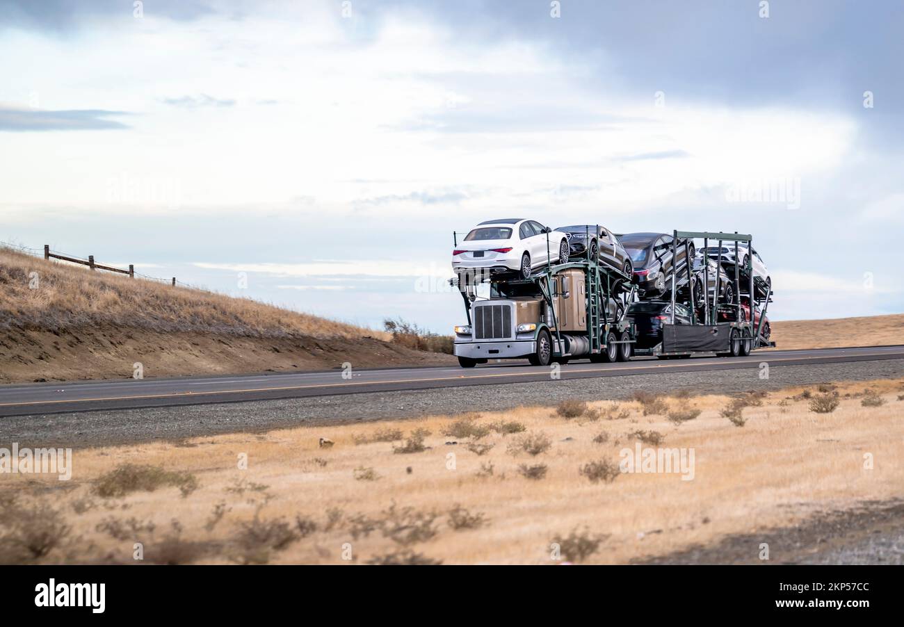 Beige commercial big rig car hauler semi truck with turned on headlight ...