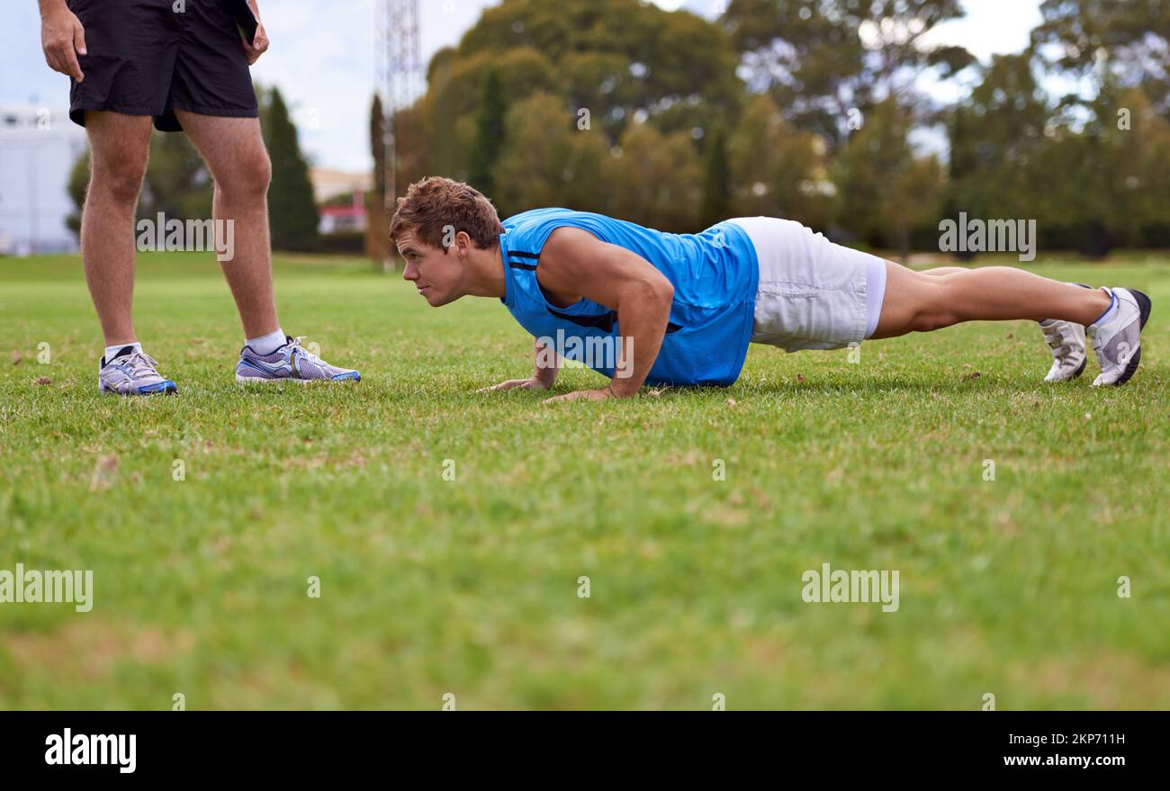 In the business of fitness. A fit young man doing push-ups on a sports field with his coach ...