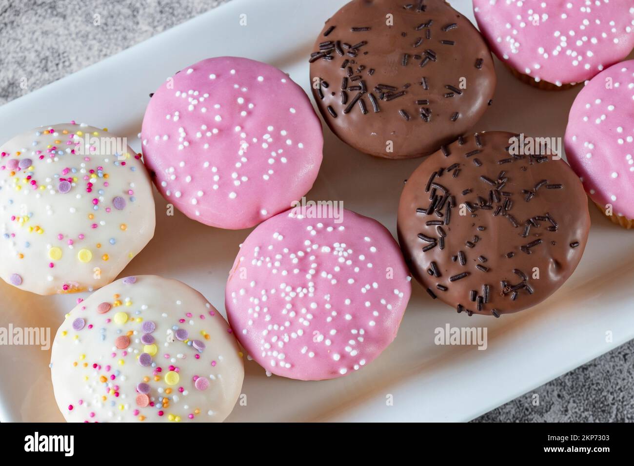 Cupcakes, decorated with icing and sprinkles on a white serving plate ...