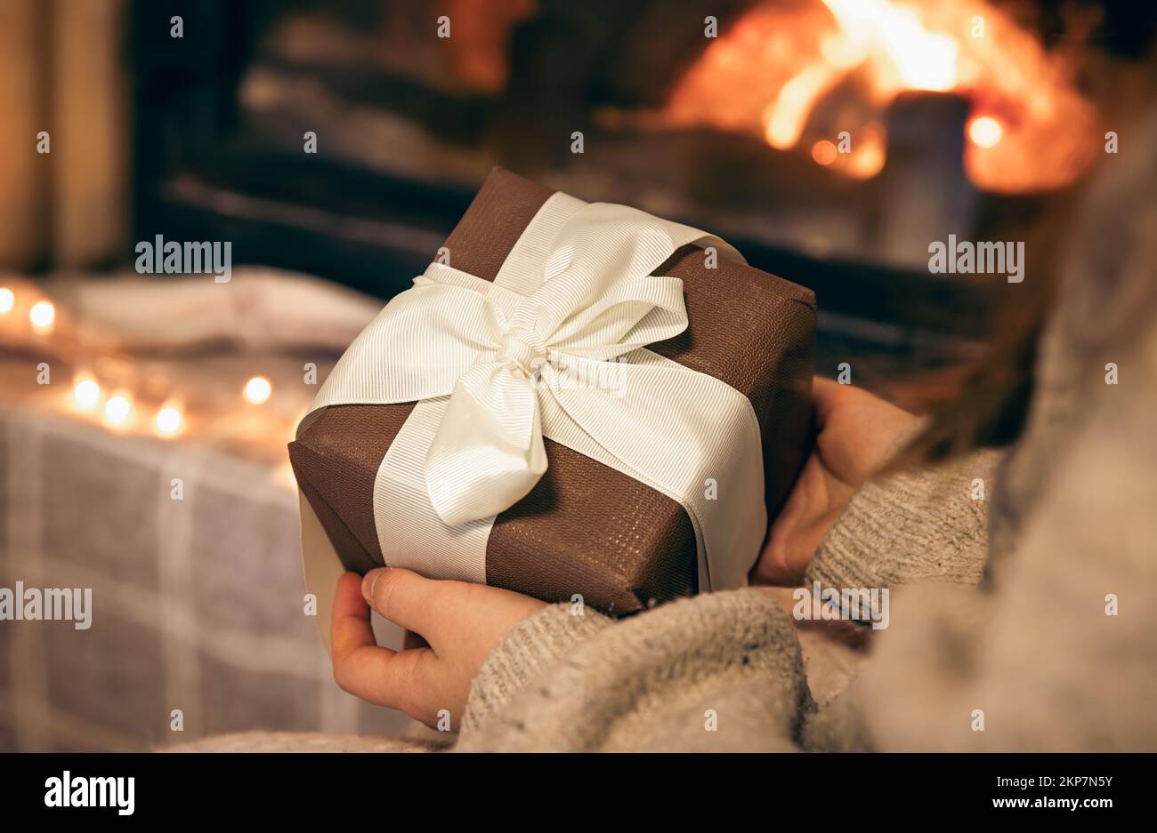 Beautiful gift box in female hands on a blurred fireplace background ...