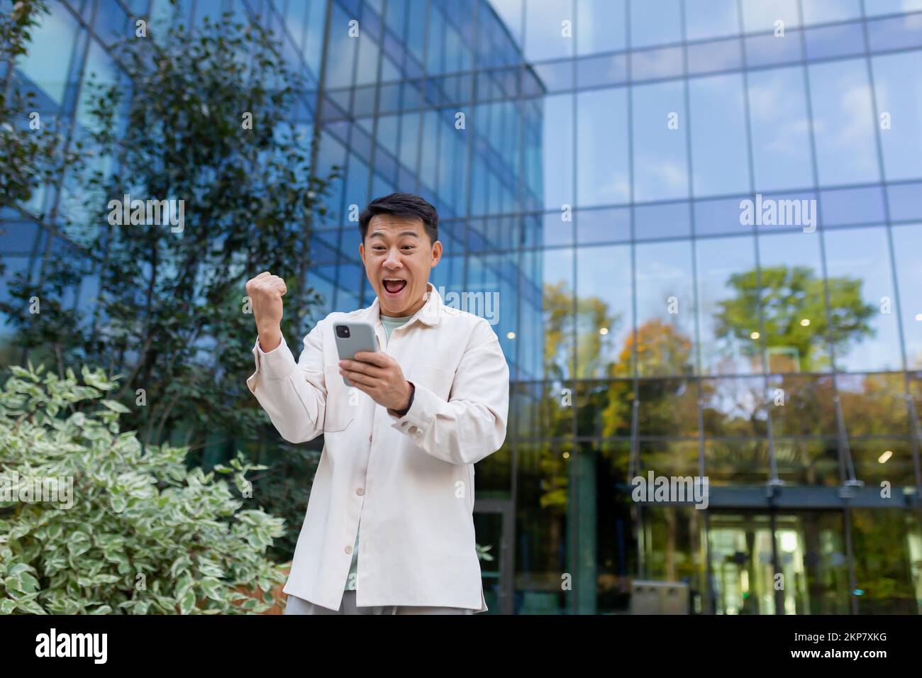 Asian businessman in casual clothes with phone outside office building ...