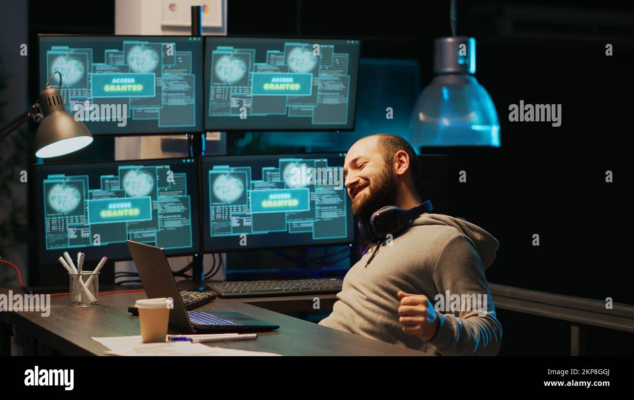 Cyber criminal celebrating hacking success in office at night, working with multiple monitors to ...