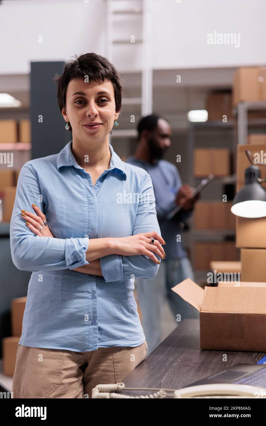 Woman supervisor standing in warehouse with arm crossed after finishing packing clients orders ...