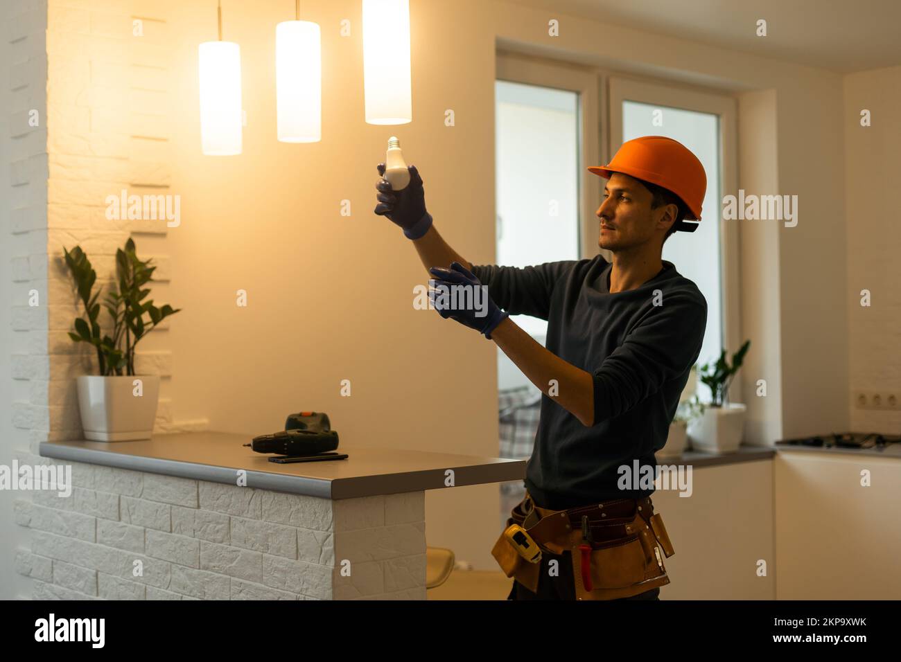 Handsome young builder in construction helmet is twisting the light ...