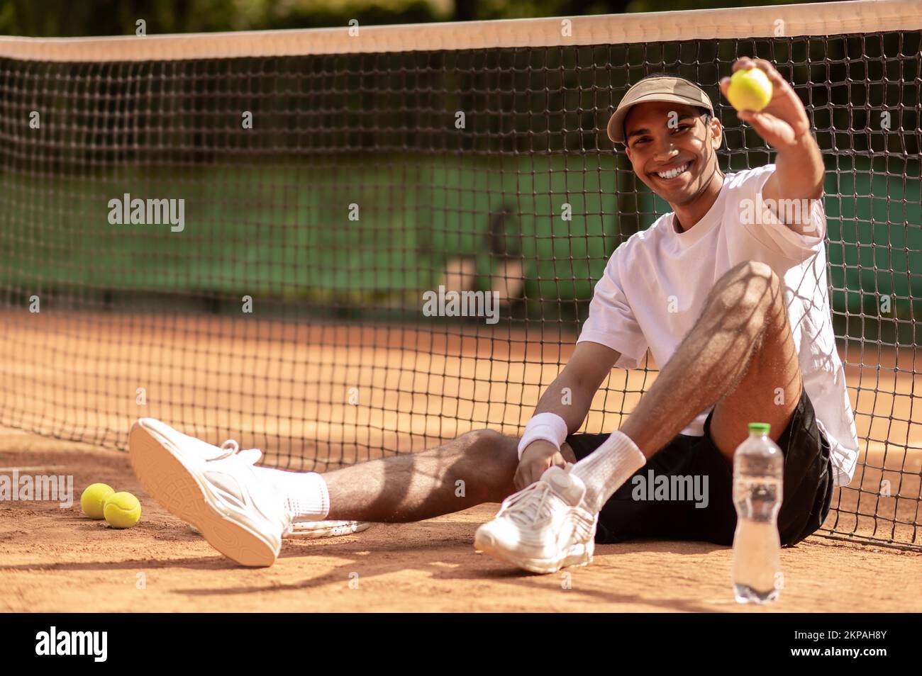 Young handsome tennis player sitting on the tennis court with a tennis ...