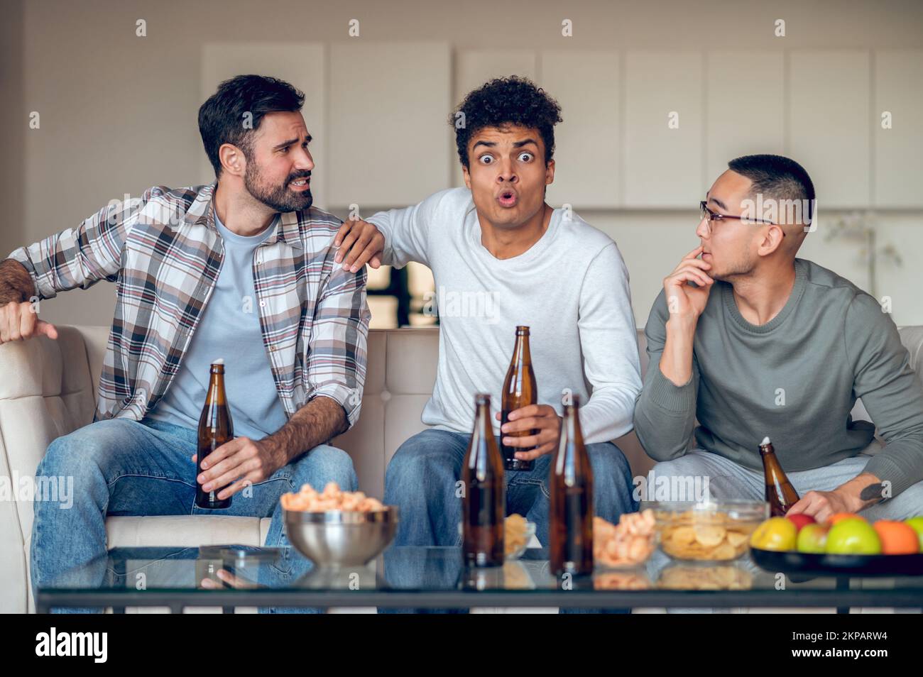 Three pals with bottles of beer sitting in the room Stock Photo - Alamy