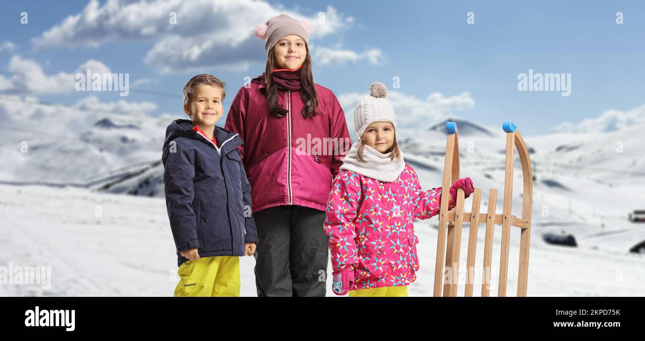 Children in winter clothes standing with a wooden sleigh on a snowy ...