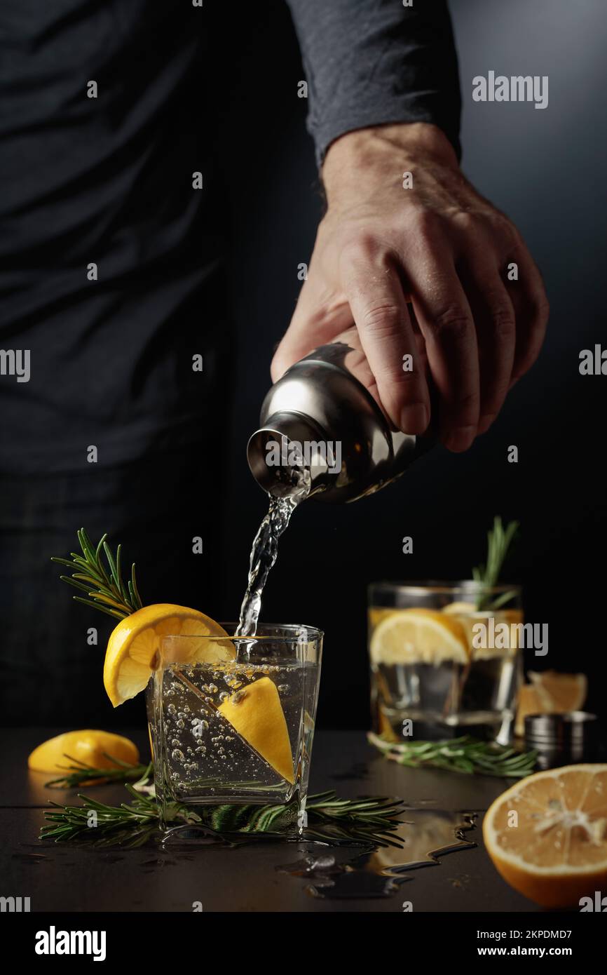 Cocktail Gin-tonic with lemon and rosemary. The bartender pours a cocktail from a shaker into a ...