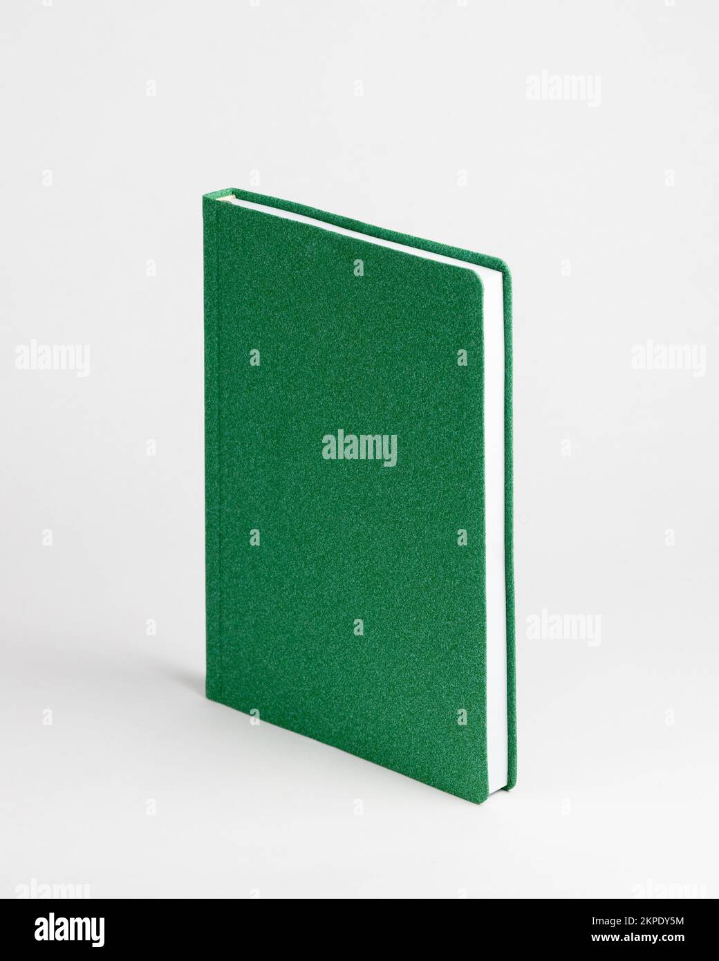 Green closed diary standing on table on white background. Side view ...