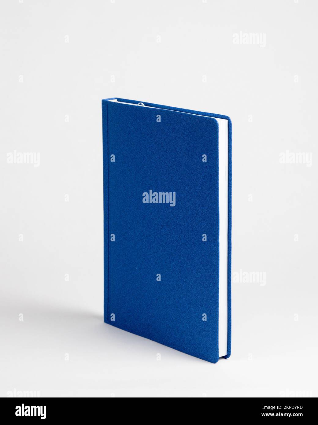 Blue closed notebook in a standing view on a white background. Side ...