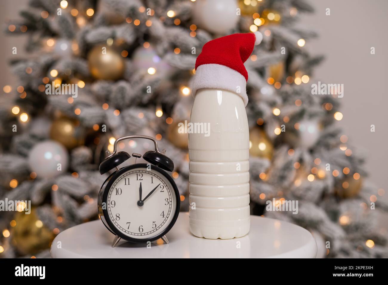 A bottle of milk with a santa claus hat and an alarm clock on the ...