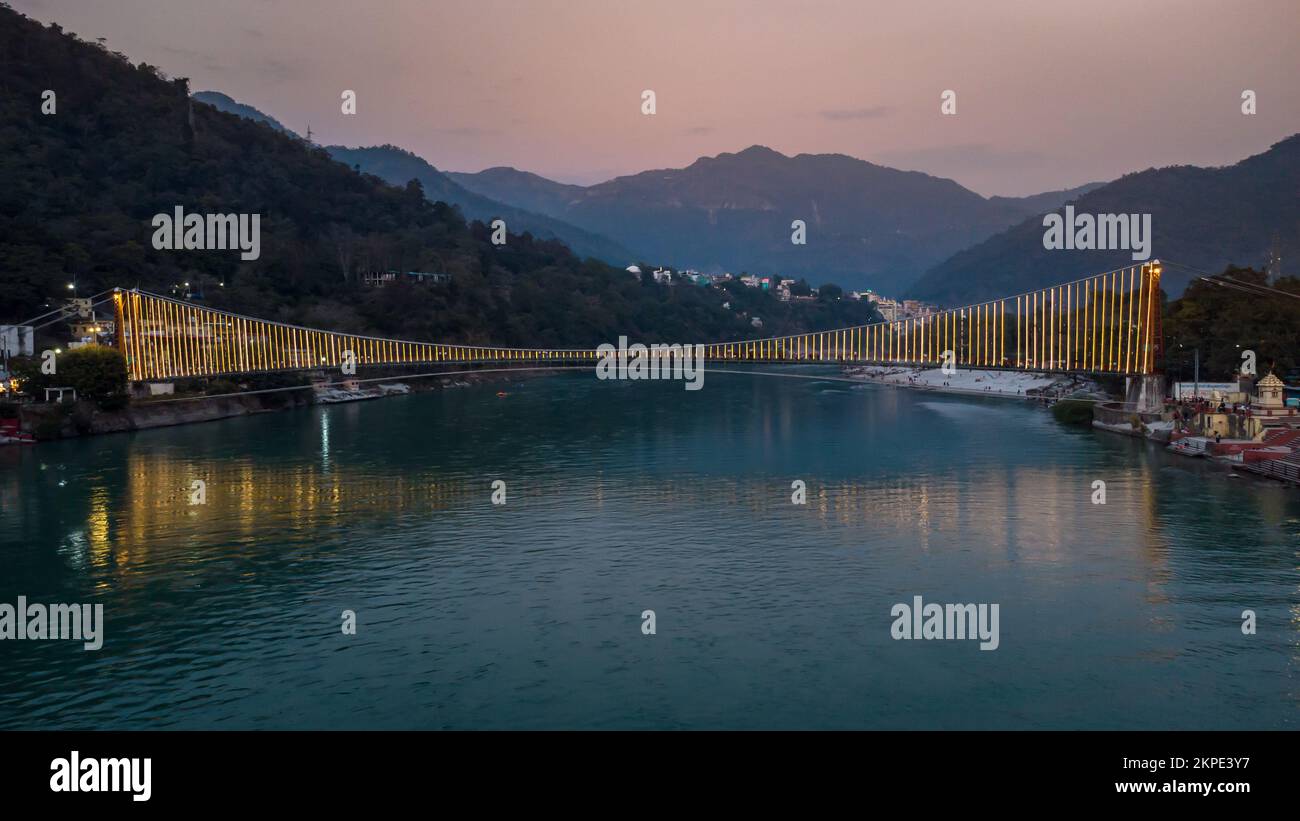 A iron suspension bridge illuminated with ferry lights over the ganges ...