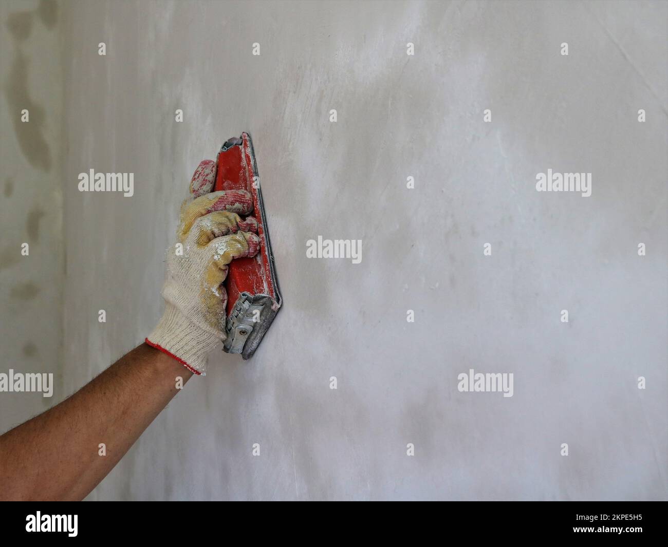 sanding the surface of a plastered wall with a hand sander close-up, a ...
