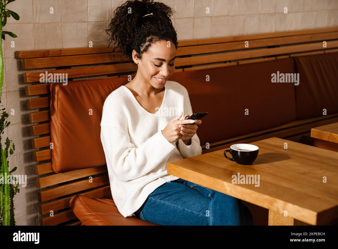 Young black woman using mobile phone while drinking coffee in cafe ...