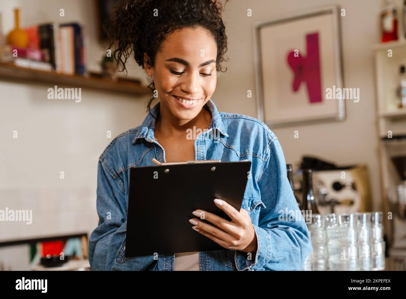 Black barista woman writing down notes while working in cafe indoors ...
