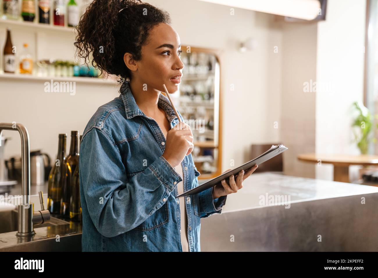Black barista woman writing down notes while working in cafe indoors ...