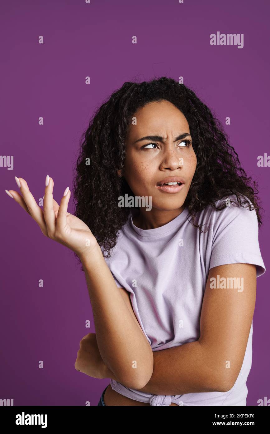 Perplexed black woman gesturing and looking aside isolated over purple ...