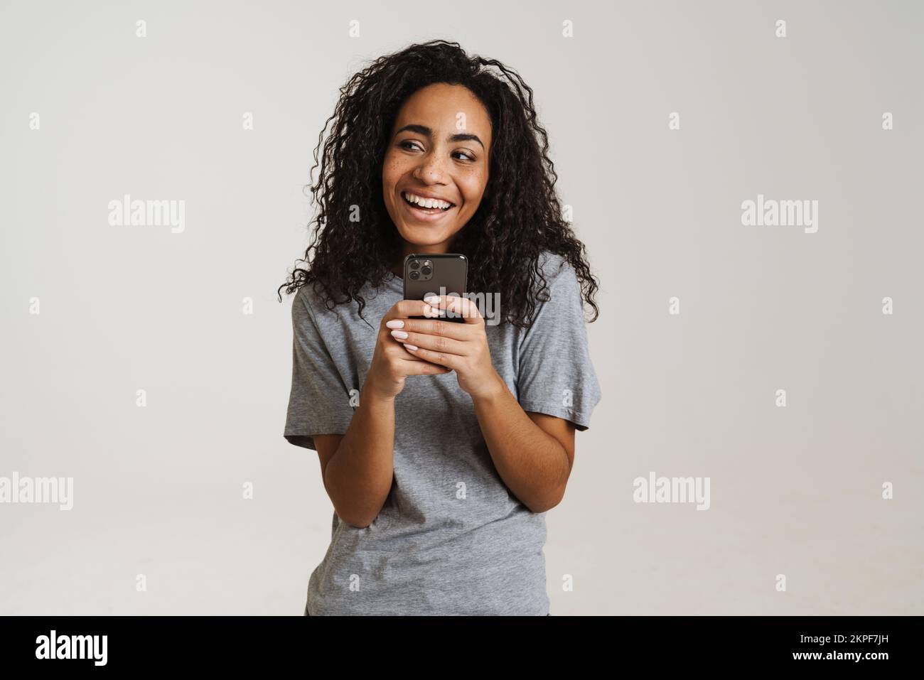 Young black woman using mobile phone and laughing isolated over white ...