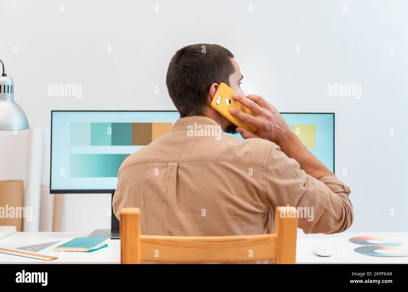 Young graphic designer sitting at his work desk and using a color ... Young graphic designer sitting at his work desk and using a color ...
